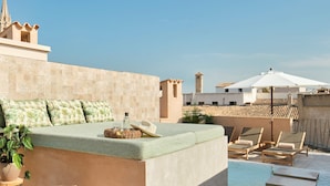 Terraço no telhado com piscina, espreguiçadeiras e vista para a torre de uma igreja.