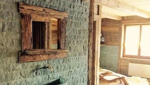 Quarto rústico com parede de pedra, moldura de janela de madeira, pia de pedra e chão de madeira.