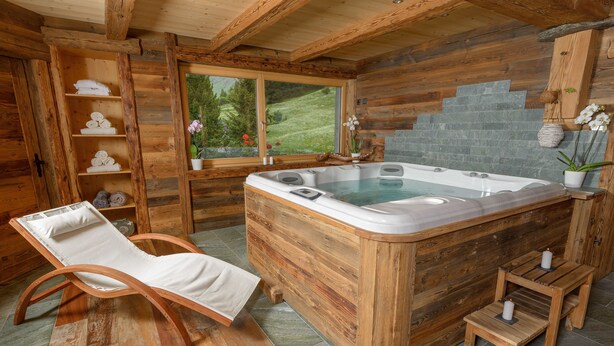 Interior de uma cabana de madeira com hidromassagem, estantes de madeira e vista para o exterior.