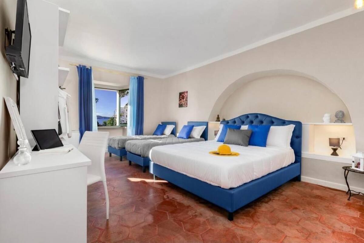 Quarto de hotel com uma cama grande, duas camas menores, uma escrivaninha e uma televisão.