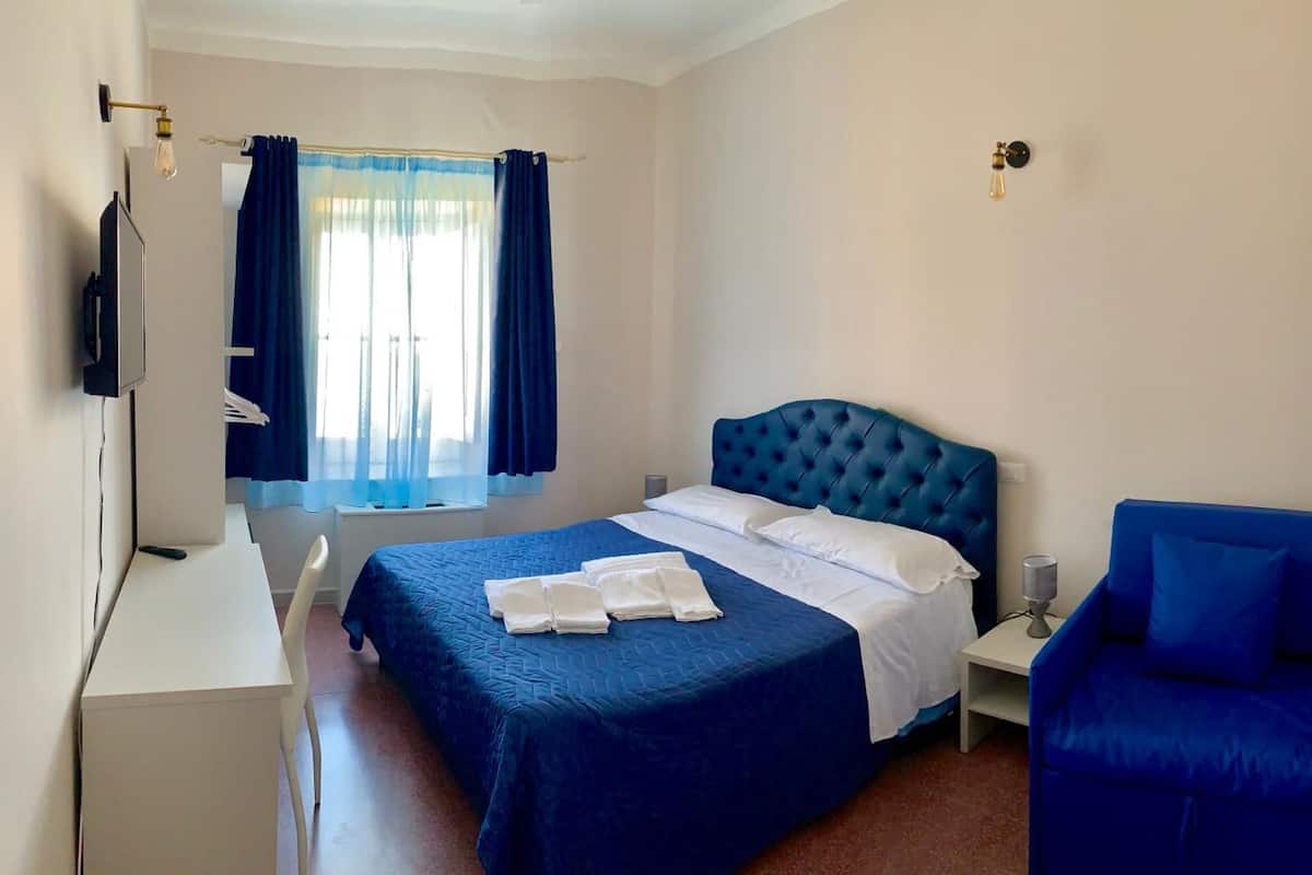 Quarto de hotel com cama, escrivaninha, cadeira e janela com cortinas.