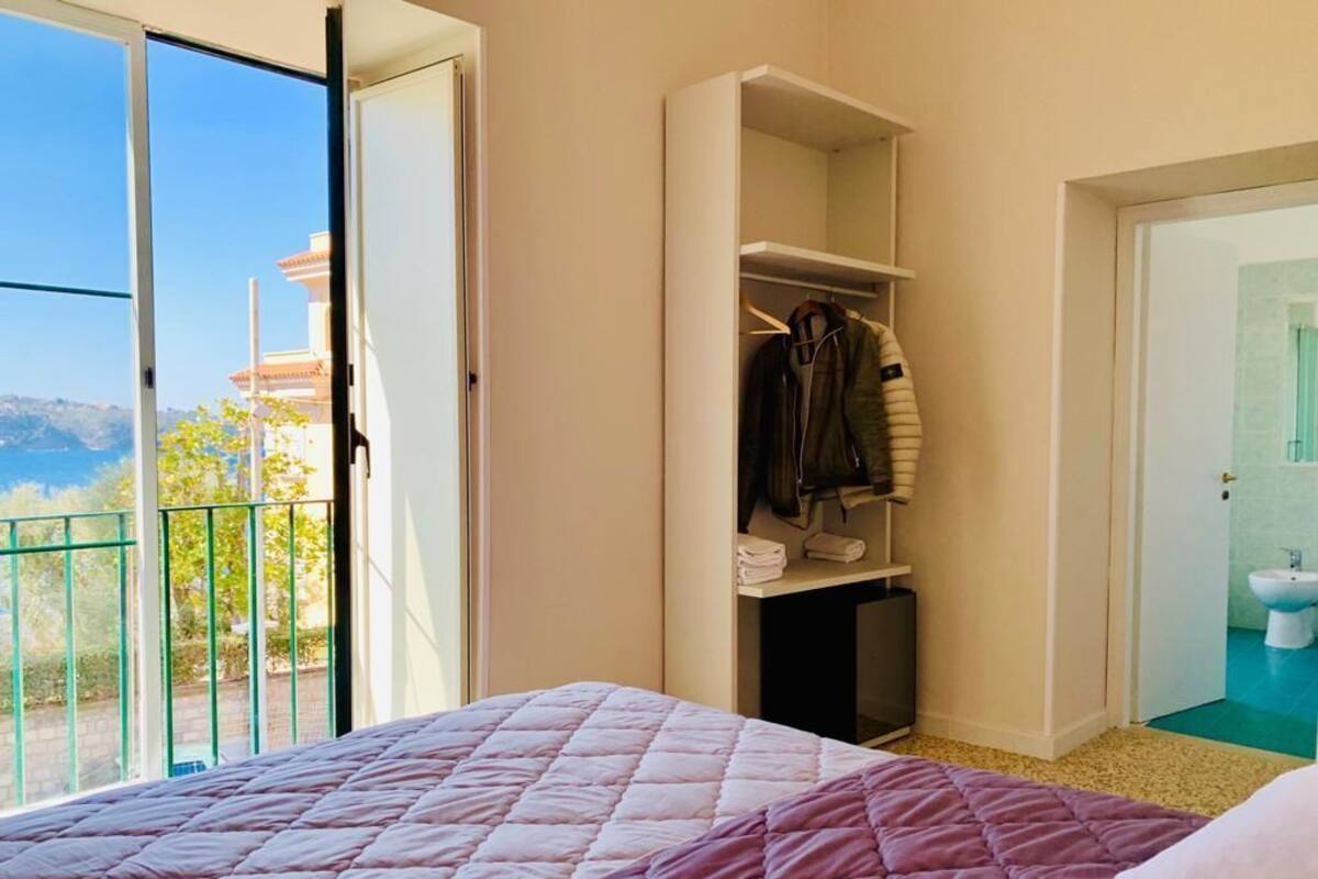 Quarto com cama, armário com roupas penduradas e banheiro com pia.