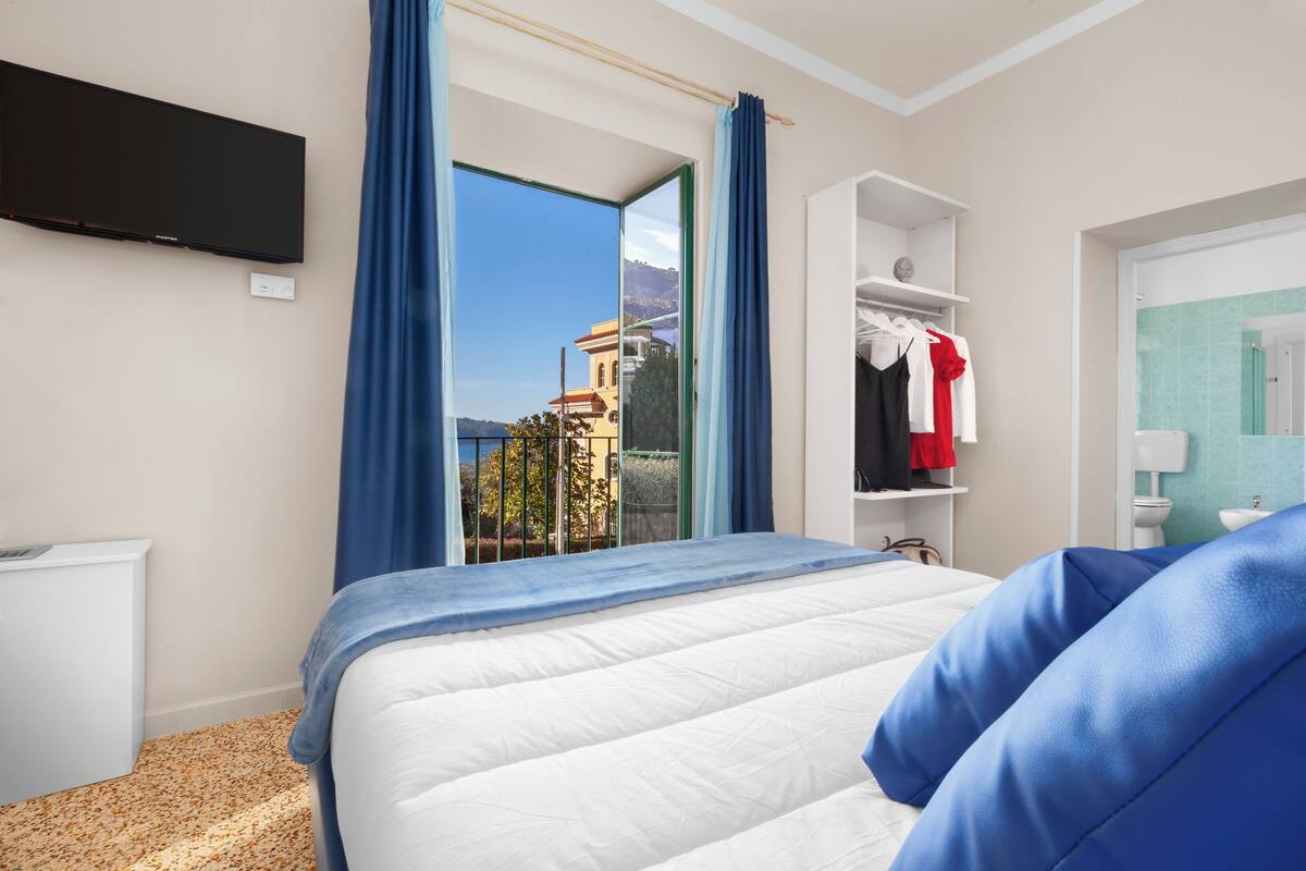 Quarto de hotel com cama, televisão na parede, guarda-roupa e banheiro com pia e espelho.
