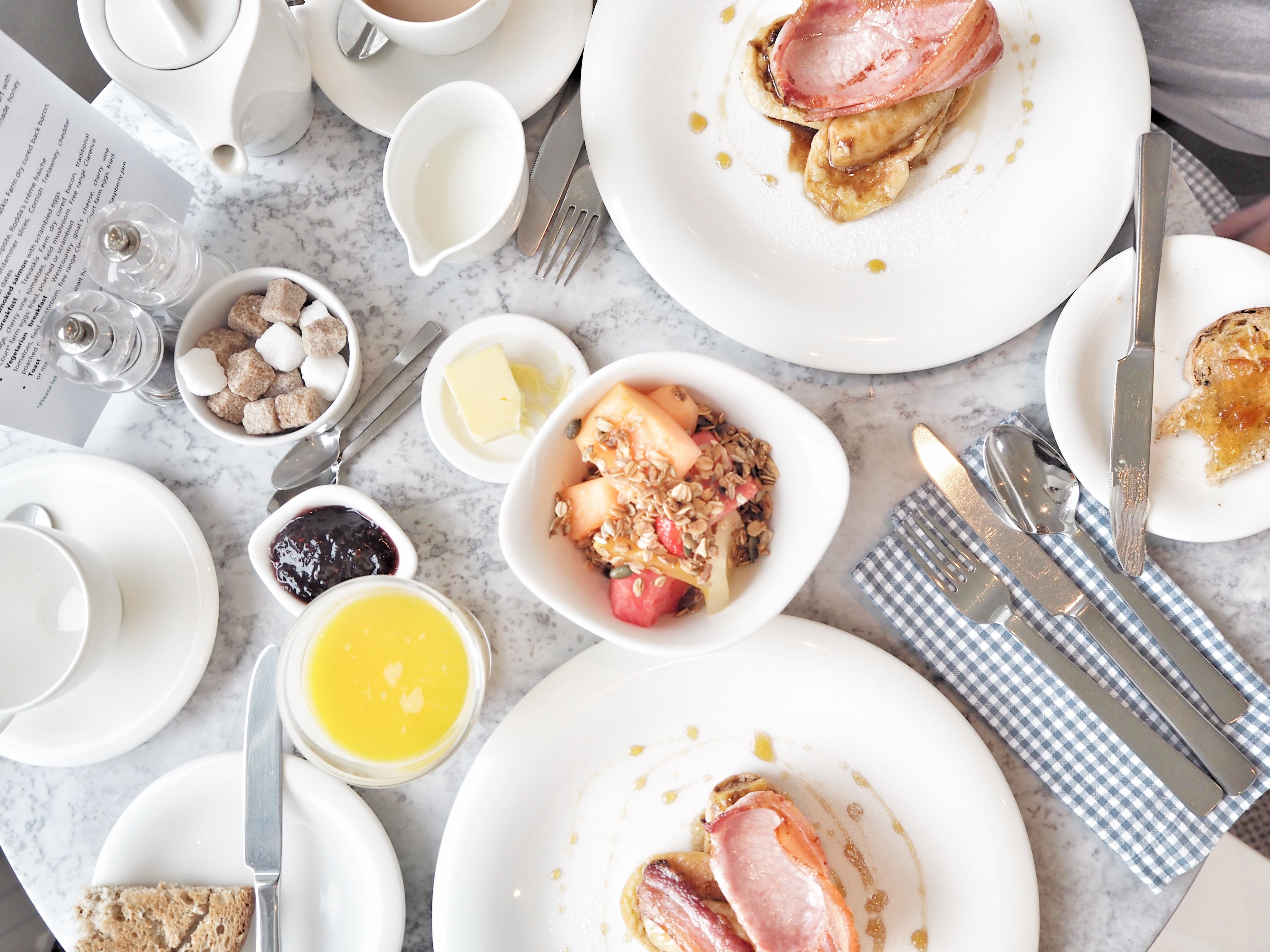 Mesa de mármore com um serviço de café da manhã variado, incluindo ovos, bacon e frutas.