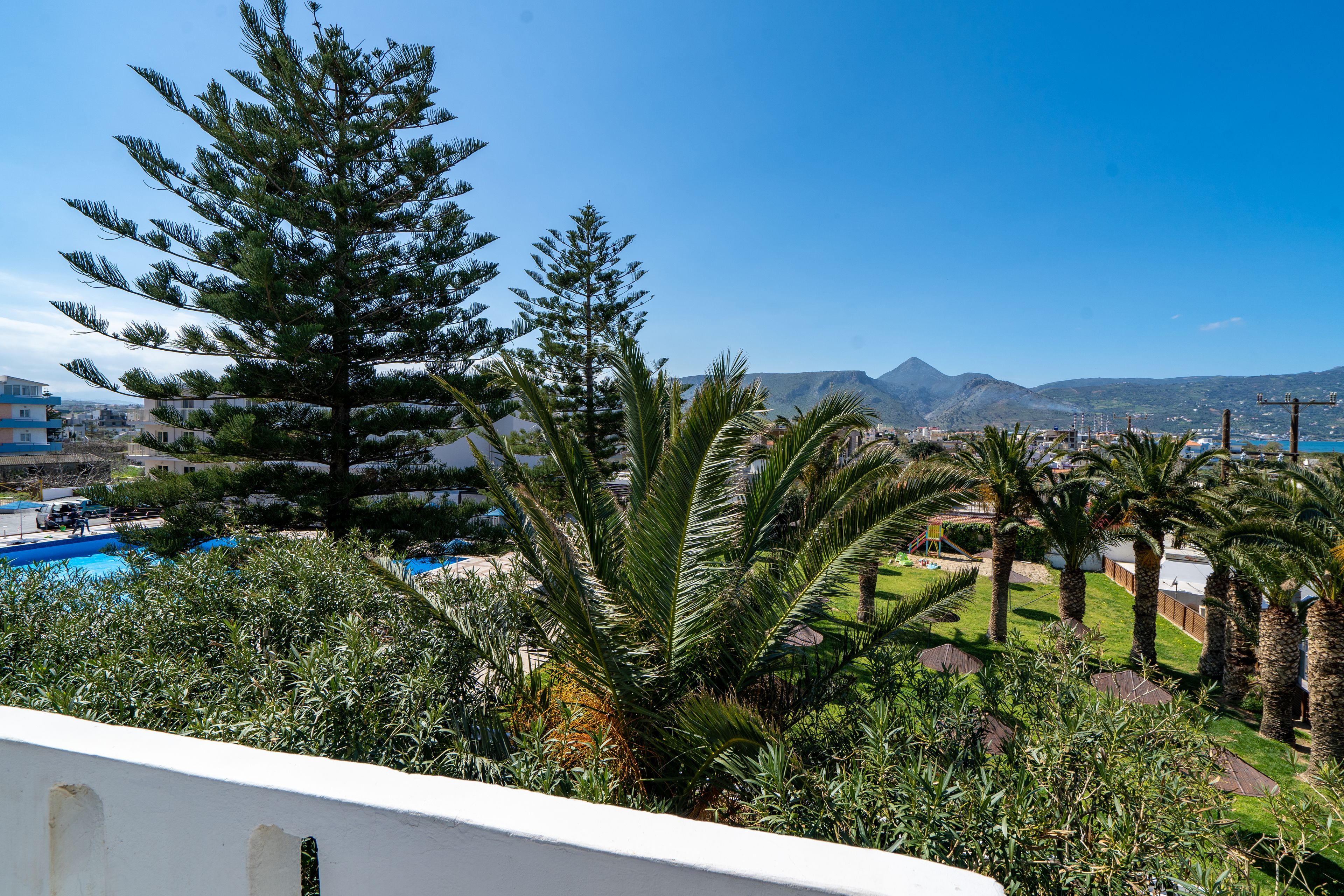 Vista de uma piscina rodeada por vegetação exuberante e palmeiras, com montanhas ao fundo.