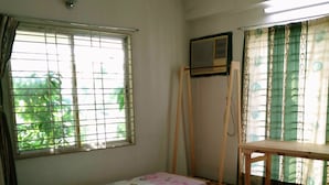 Quarto com duas camas de madeira, roupa de cama colorida, um ventilador e uma janela com cortina.