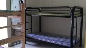 Uma cama de beliche com cama inferior e escada de madeira, um pequeno armário de madeira e um ventilador de teto.