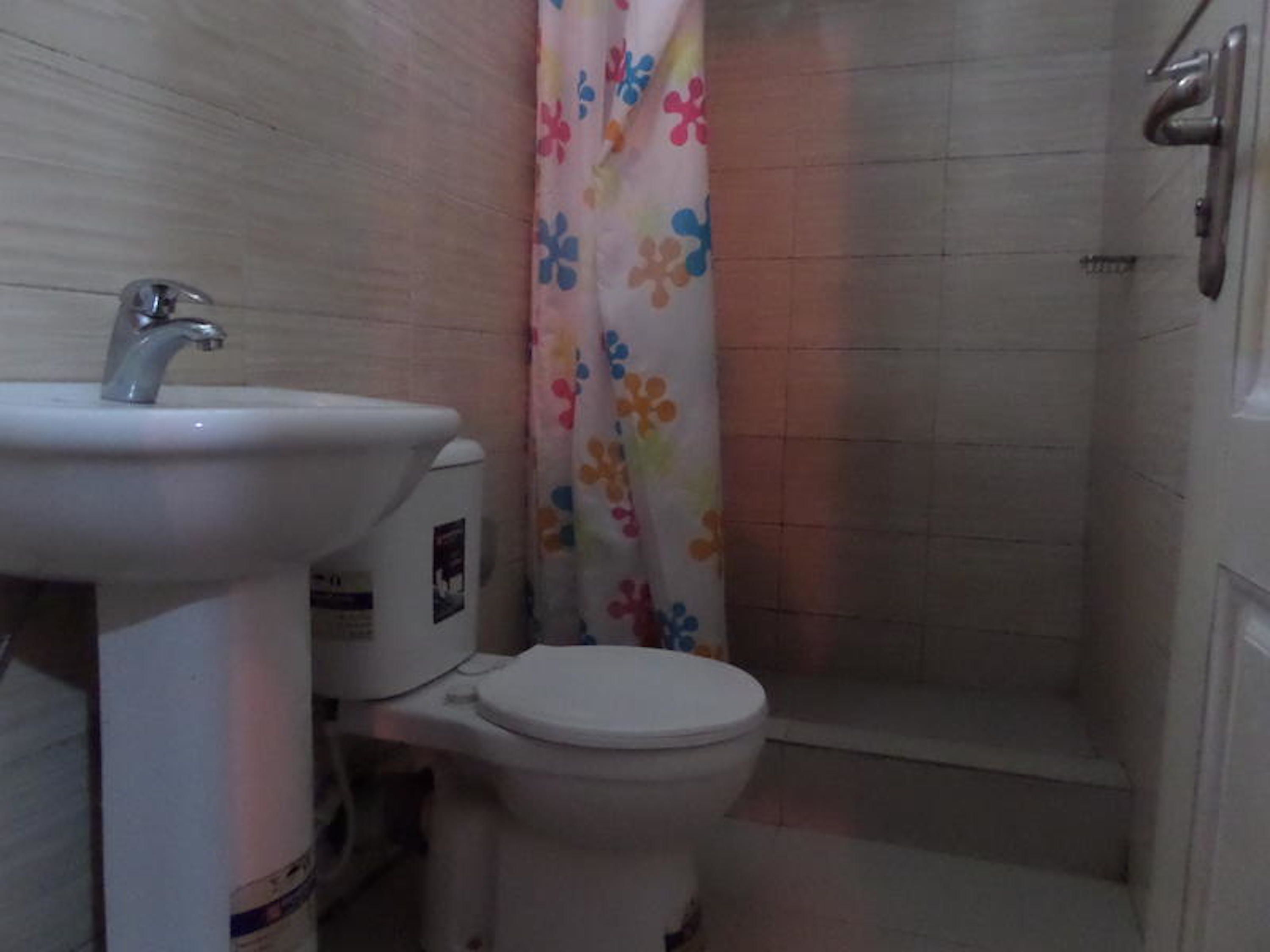 Casa de banho com lavatório branco, sanita e cortina de chuveiro com padrão floral.