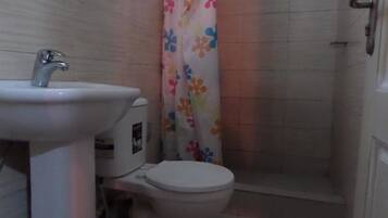 Casa de banho com lavatório branco, sanita e cortina de chuveiro com padrão floral.