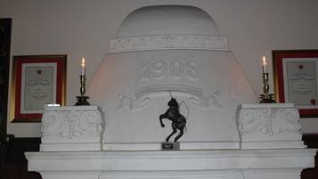 Lareira branca com estátua de cavalo, o ano 1908 e duas velas acesas.