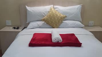 Cama bem arrumada com roupa de cama branca e vermelha, almofada estampada e toalha enrolada.