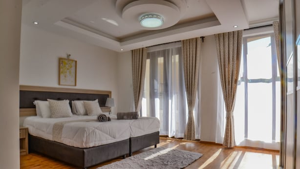 Quarto moderno com uma cama grande, uma mesa de cabeceira e uma janela com cortinas.