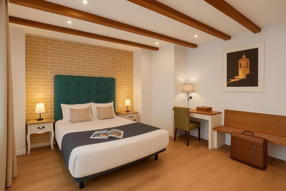 Quarto de hotel com uma cama grande, uma escrivaninha, uma cadeira, um abajur e um quadro na parede.