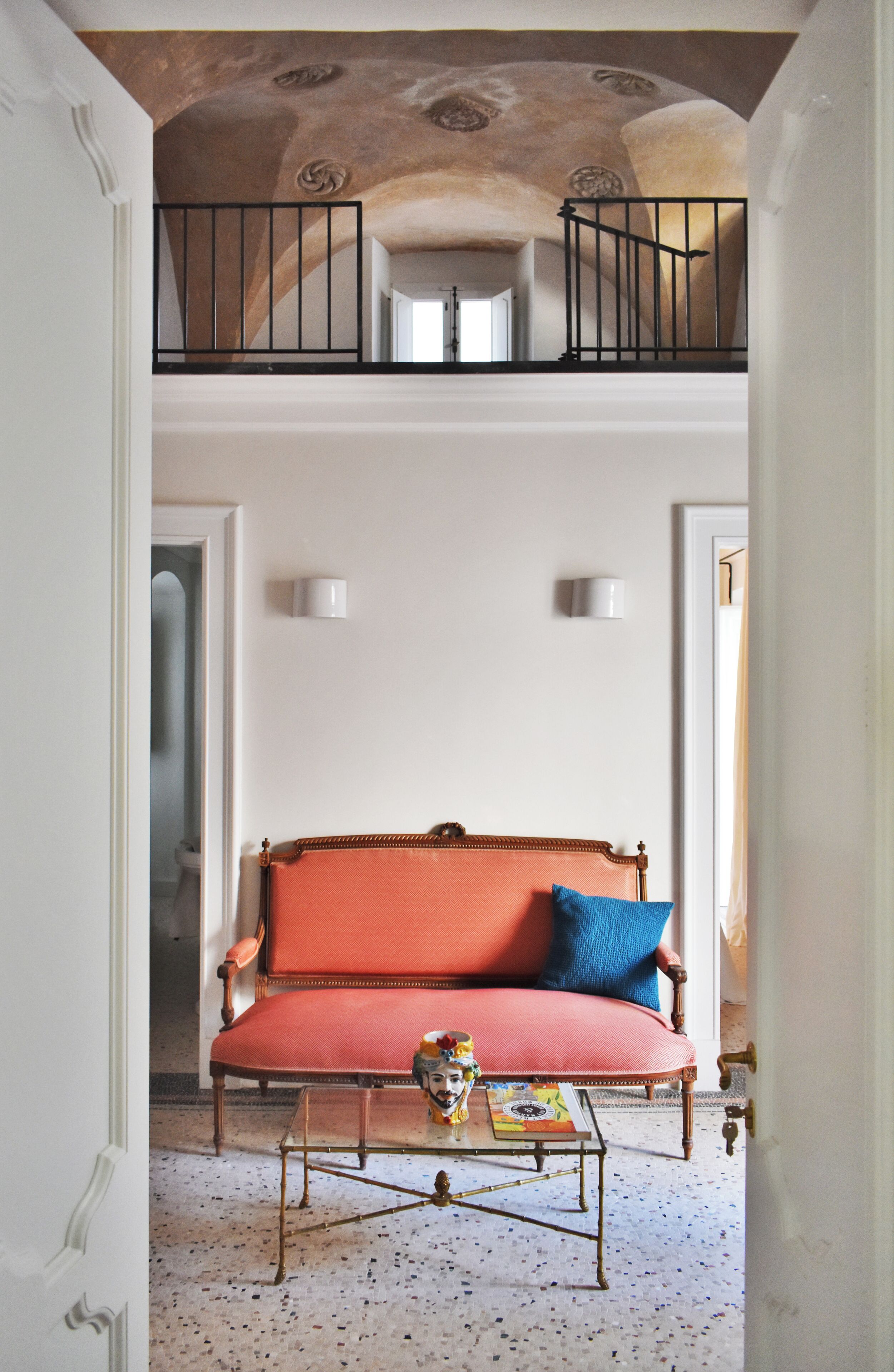 Um quarto com um sofá vermelho, uma mesa pequena e uma máscara decorativa no chão.