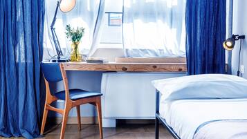Um quarto com uma cama, uma escrivaninha com cadeira, uma luminária e uma janela com cortinas.