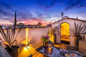 Terraço no telhado com vista para o pôr do sol, plantas em vasos, uma mesa com velas e um espaço de estar acolhedor.