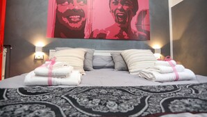 Quarto de hotel com cama, travesseiros e um pôster grande na parede.
