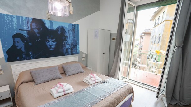 Quarto com cama grande, pintura na parede, guarda-roupa e varanda com vista para prédios.