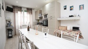 Uma cozinha moderna com armários brancos, uma mesa de jantar com cadeiras e uma TV fixada na parede.