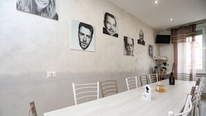 Uma sala de jantar com uma mesa comprida, cadeiras brancas e obras de arte fixadas na parede.