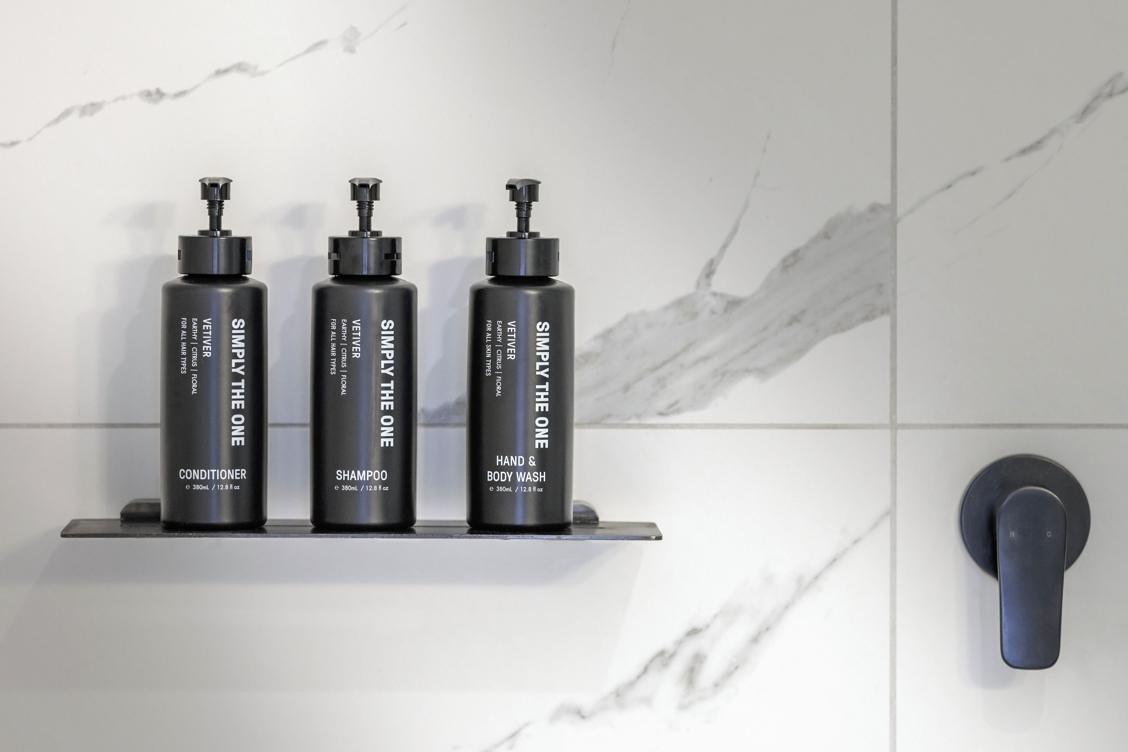 Três frascos pretos de produtos VETIVER em uma prateleira, em frente a uma parede de mármore.