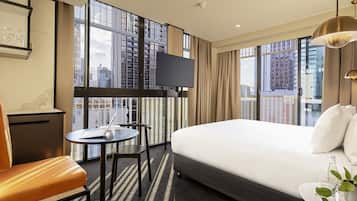 Quarto de hotel com uma cama grande, uma escrivaninha, uma cadeira e uma televisão.