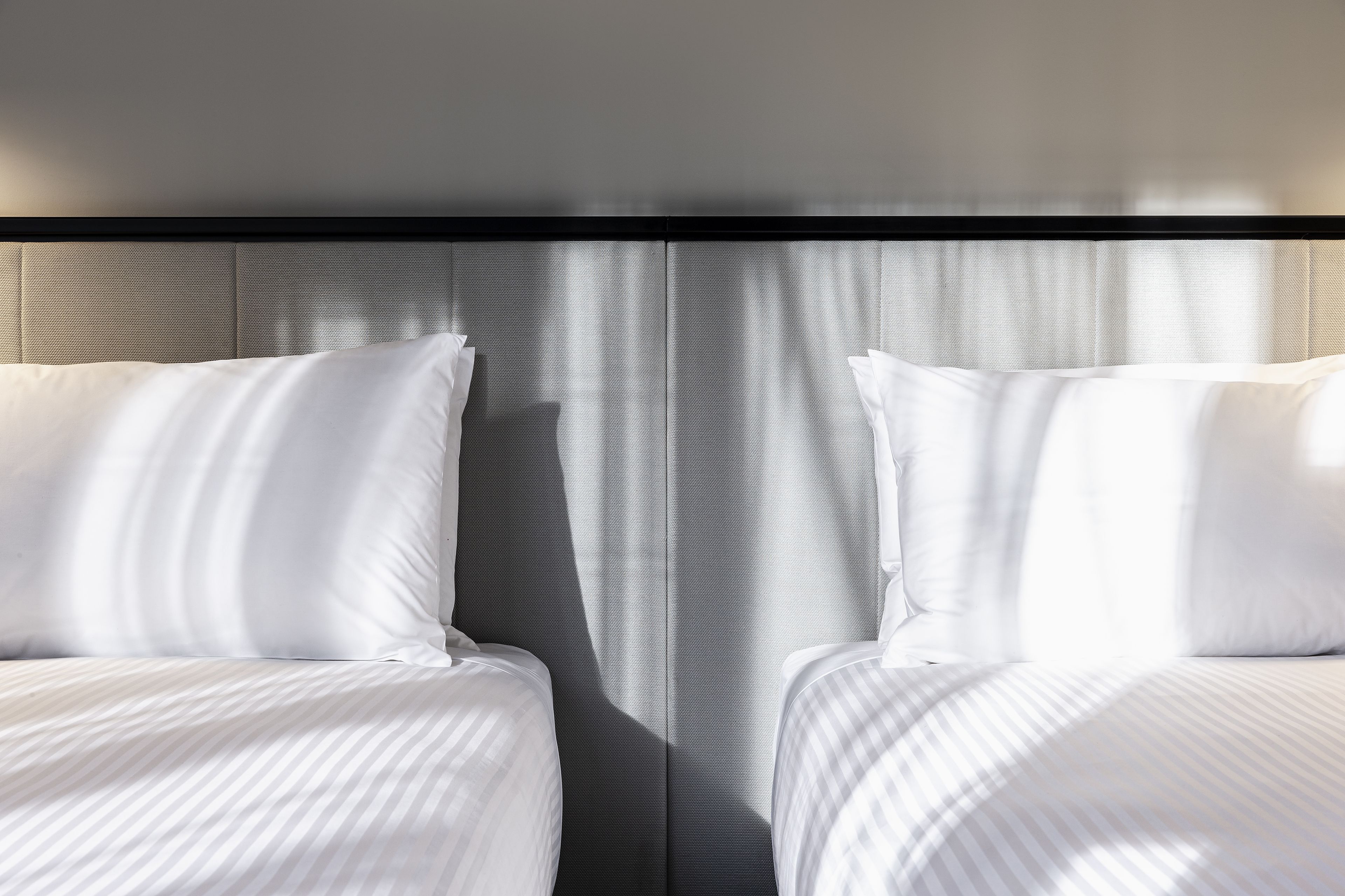 Quarto de hotel com duas camas, cabeceira e janela com cortinas.