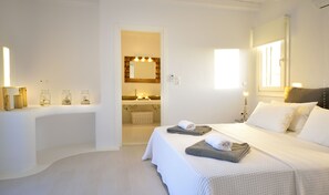 Quarto de hotel com uma cama grande, banheiro com pia e espelho, e vista para o mar.