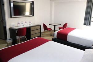 Quarto de hotel com cama, secretária com cadeiras, televisão e uma pequena mesa.