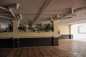 Um espaço de estacionamento interno com piso de azulejos, canos no teto e plantas em vasos ao longo das paredes.
