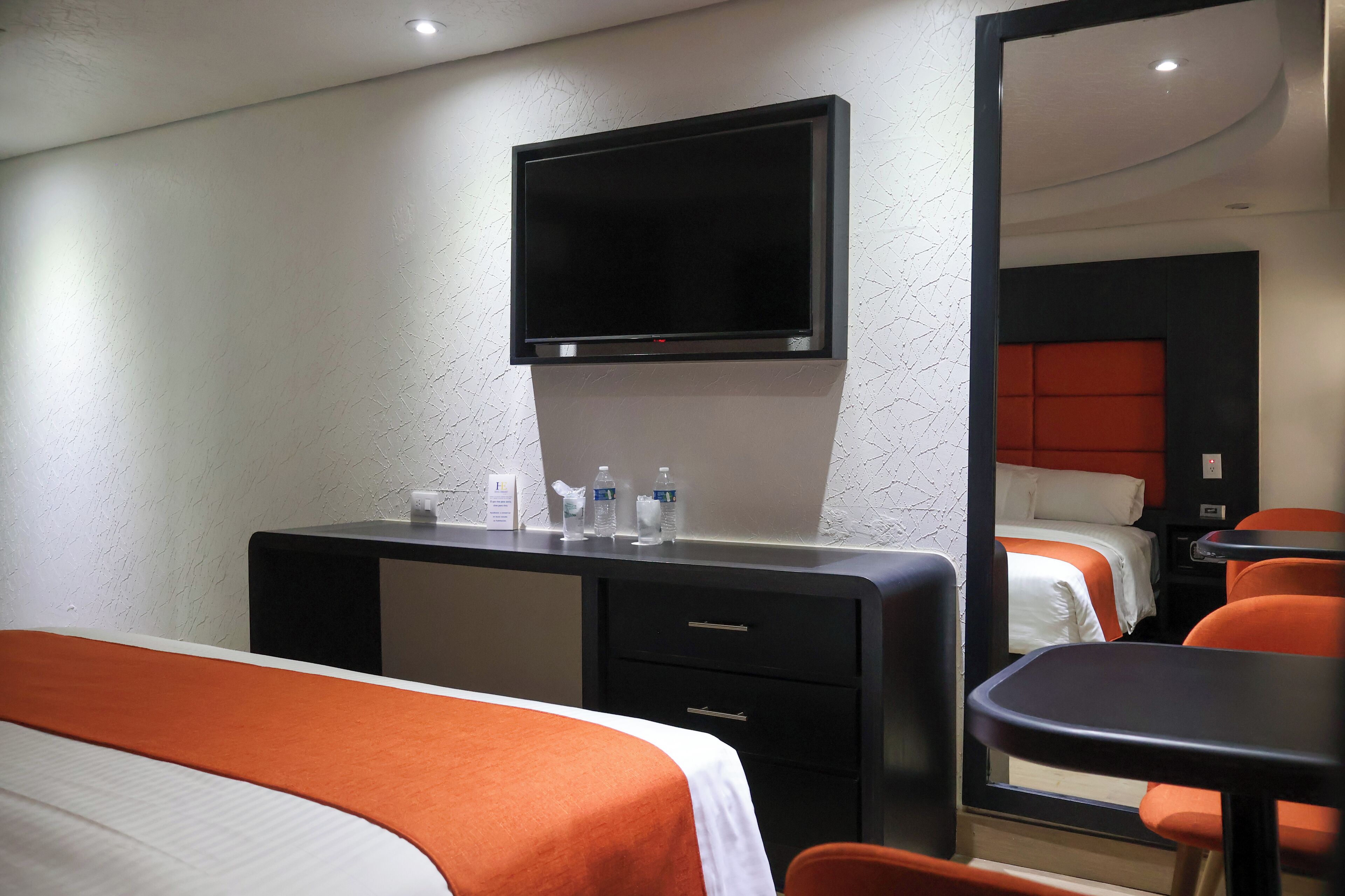 Quarto de hotel com cama, secretária, televisão de tela plana, espelho e uma pequena mesa.