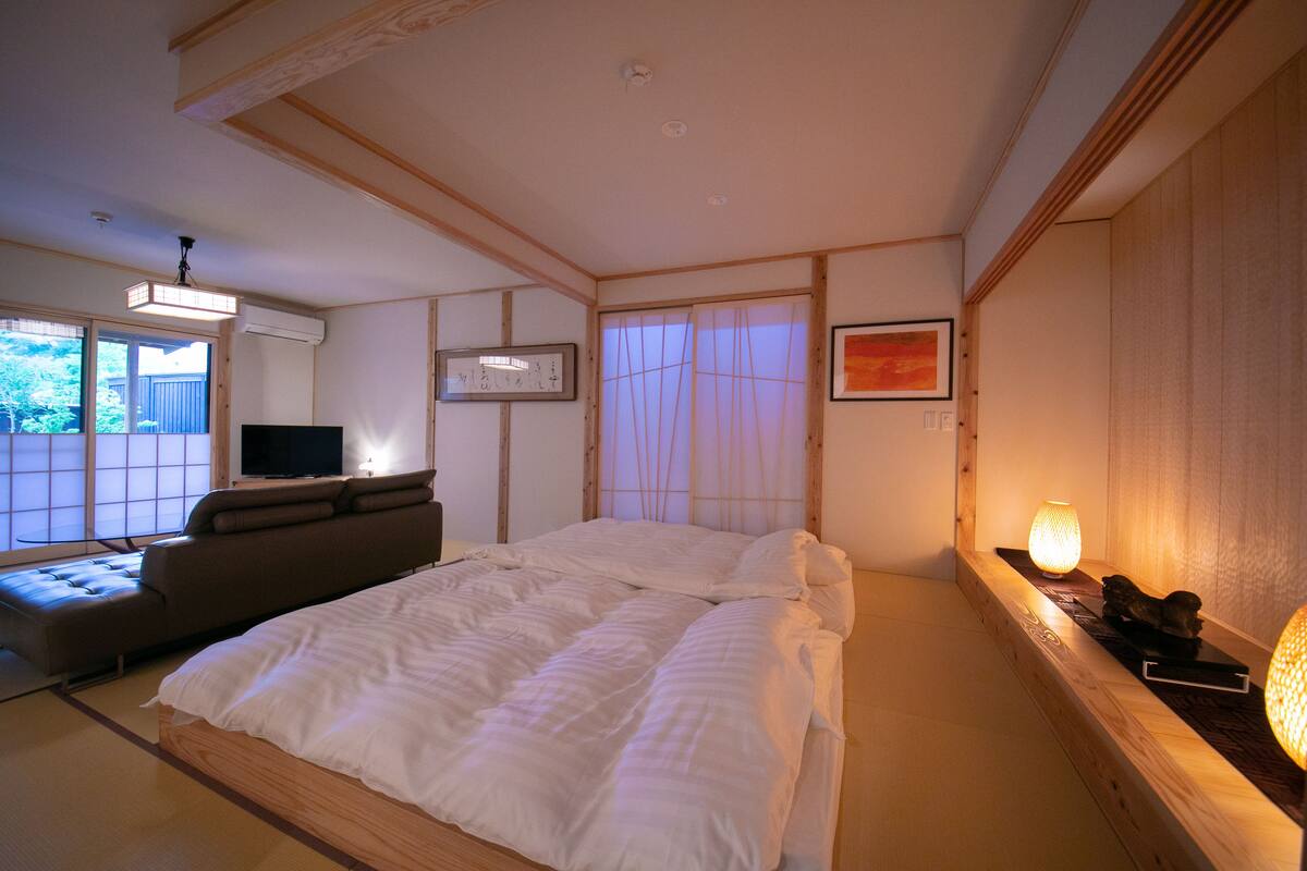 Quarto com cama, televisão, sofá, janela e mesa de cabeceira com abajur.