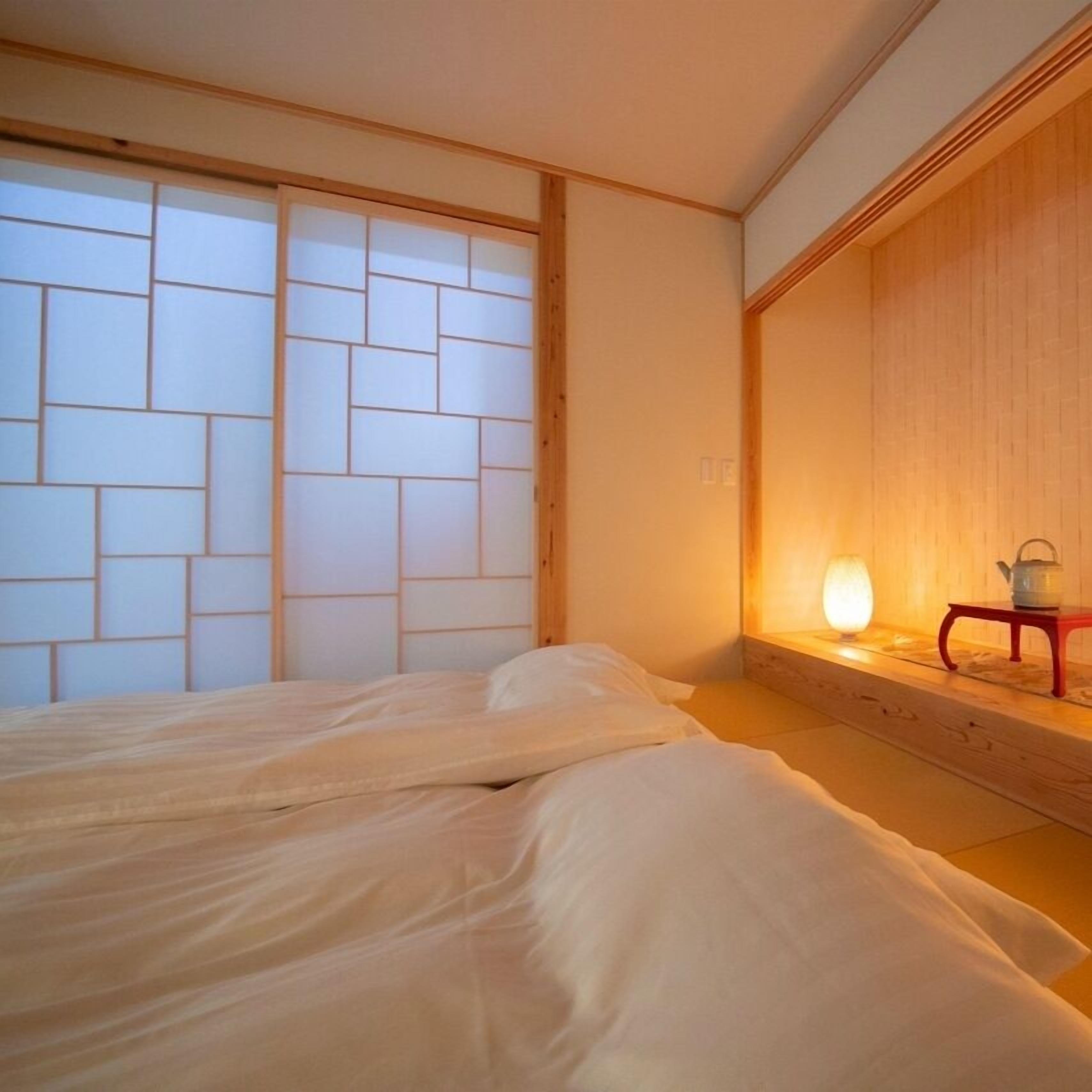 Quarto com cama, prateleira de madeira com abajur e porta deslizante com padrão geométrico.