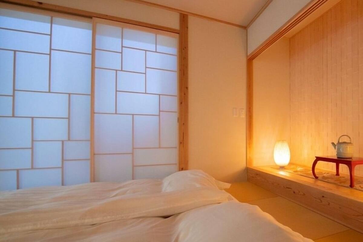 Quarto com cama, prateleira de madeira com abajur e porta deslizante com padrão geométrico.