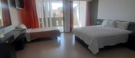 Quarto de hotel com cama, escrivaninha, televisão e varanda com cortinas.