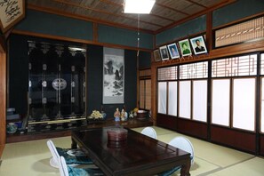 Um quarto japonês tradicional com tatames, uma mesa de madeira escura e um painel shoji com fotografias emolduradas.