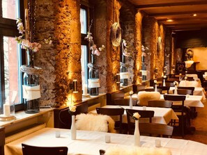 Um restaurante com paredes de pedra, mesas brancas e centros de mesa florais.