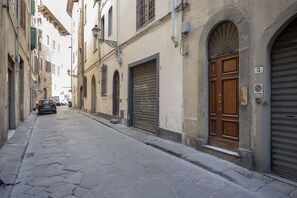 Uma rua de paralelepípedos estreita, flanqueada por edifícios históricos, com portões de lojas fechadas e um carro estacionado.