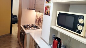 Cozinha compacta com fogão a gás, micro-ondas e chaleira.