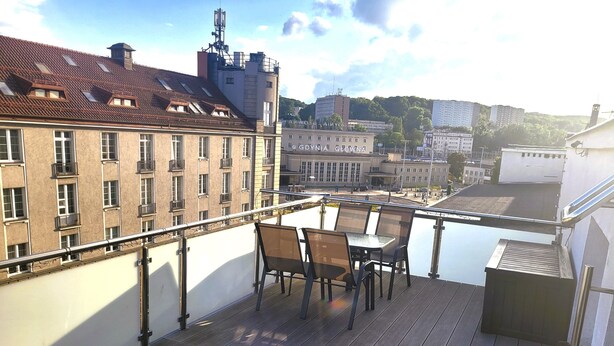 Uma varanda com mesa e cadeiras, com vista para um horizonte urbano com edifícios e uma colina ao fundo.