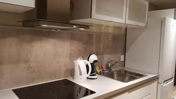 Uma cozinha moderna com armários brancos, coifa de aço inoxidável, fogão por indução, cafeteira e pia.