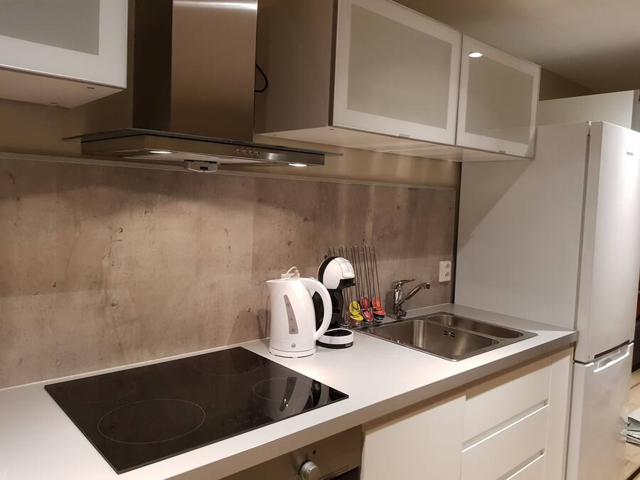 Uma cozinha moderna com armários brancos, coifa de aço inoxidável, fogão por indução, cafeteira e pia.