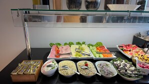 Buffet com diversos alimentos, incluindo carnes, queijos, saladas e frutas.