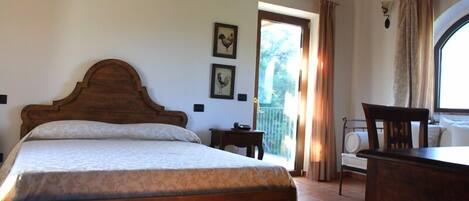 Quarto com cama de madeira, uma mesinha, uma cadeira e varanda com vista para vegetação.
