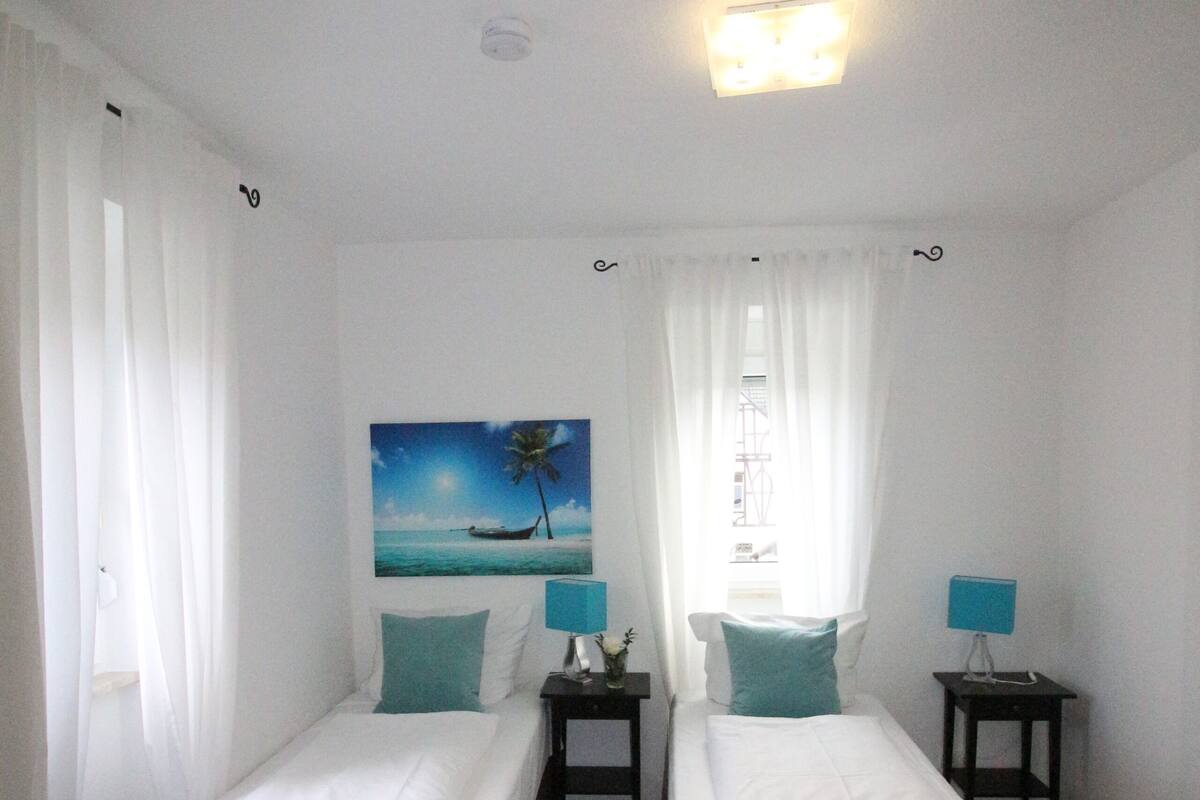 Quarto com duas camas, um quadro de uma praia e uma janela com cortinas.