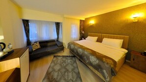 Quarto de hotel com cama, sofá, escrivaninha e janela com cortinas.