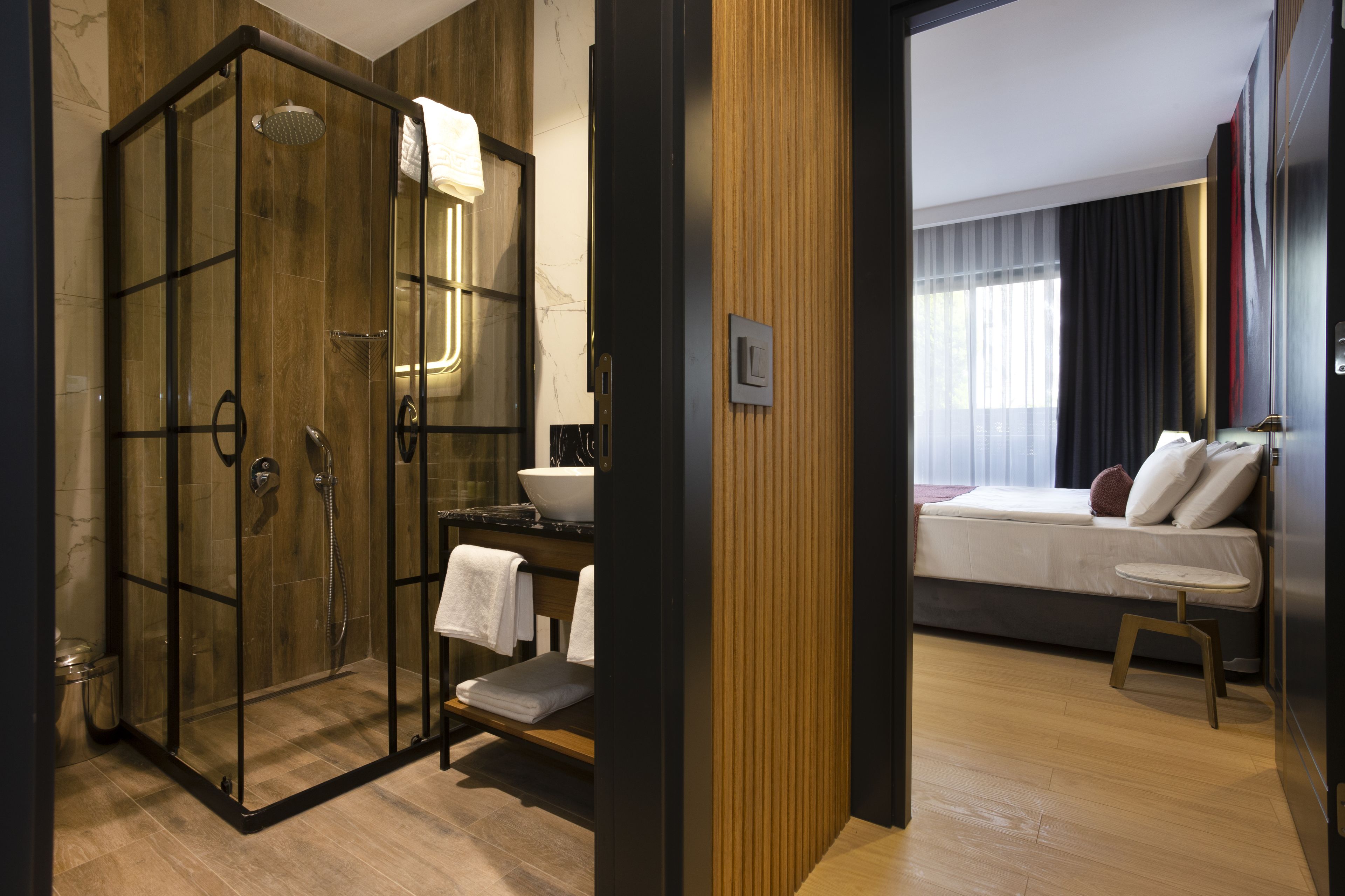 Quarto de hotel moderno com chuveiro em gabinete de vidro, toucador de madeira, cama com vista e uma pequena mesa.