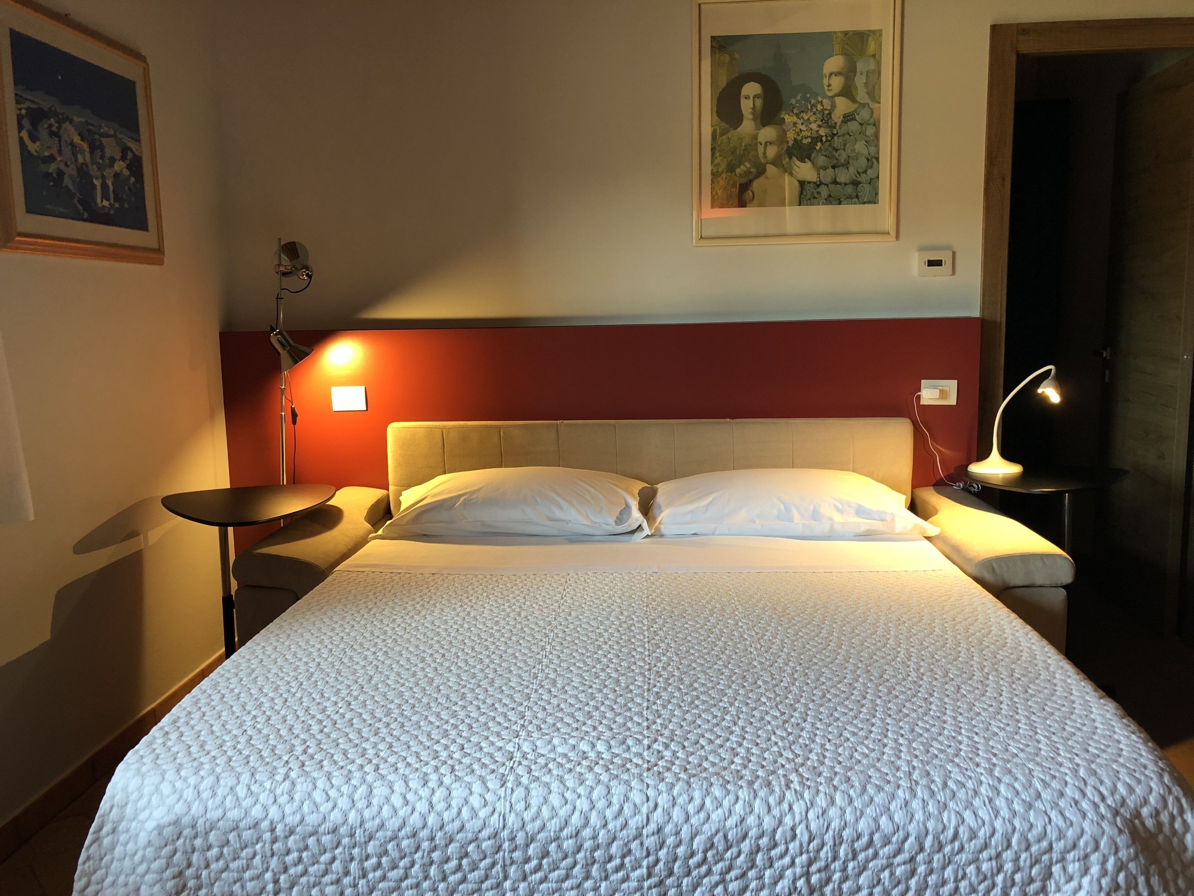 Cama bem arrumada com roupa de cama branca, parede vermelha e um quadro emoldurado acima.