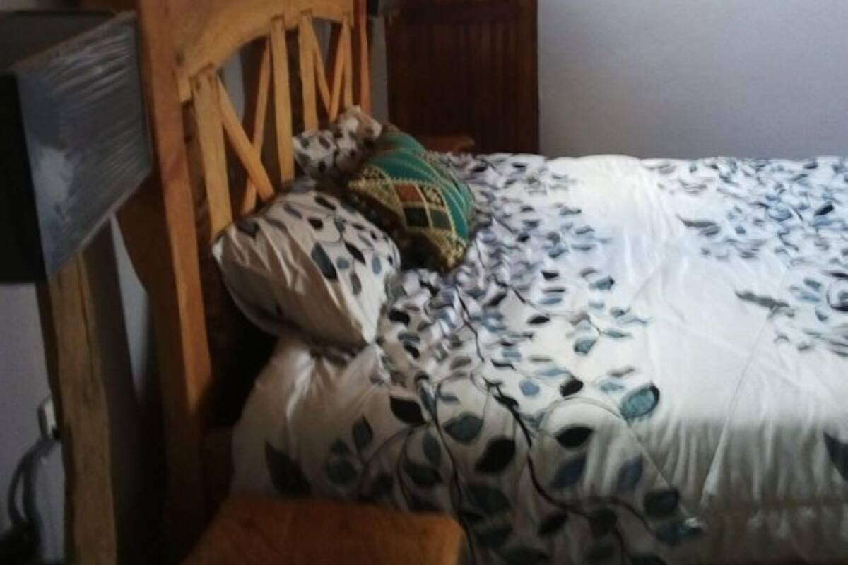 Quarto com cabeceira de madeira, cama com roupa de cama estampada, mesa de cabeceira e porta de madeira.