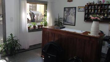 Uma área de recepção com uma mesa de madeira, um relógio, plantas em vasos e uma janela com cortinas.